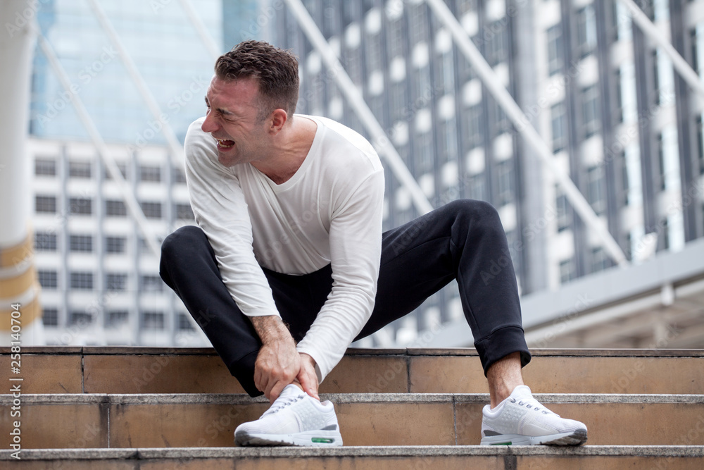 fitness man have twisted ankle pain sitting on steps of stair in the ...