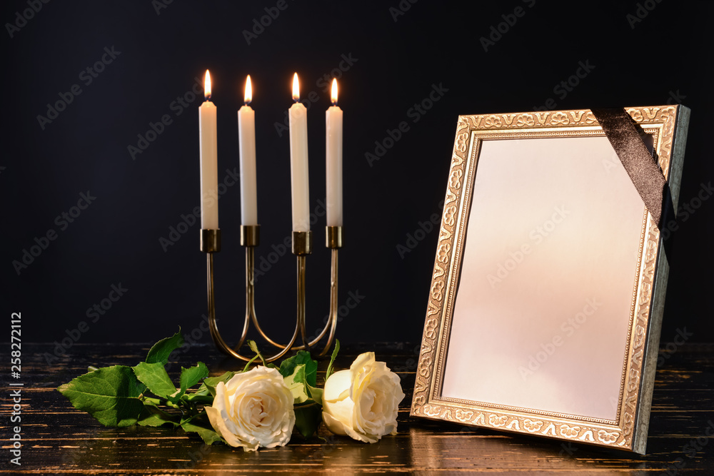 Blank funeral frame, candles and flowers on table against black ...