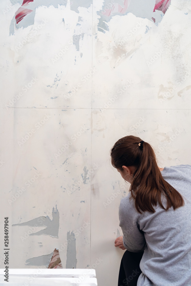 woman tears off Wallpaper, removing Wallpaper from the wall with a ...