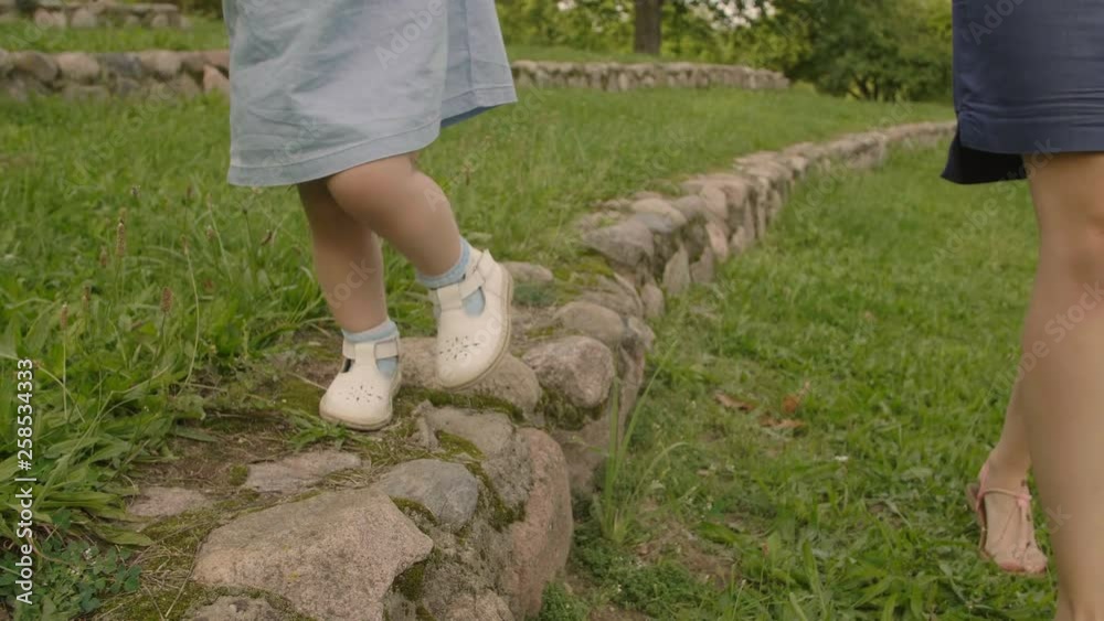 Close-up of small baby feet in white sandals walking on the stone ...