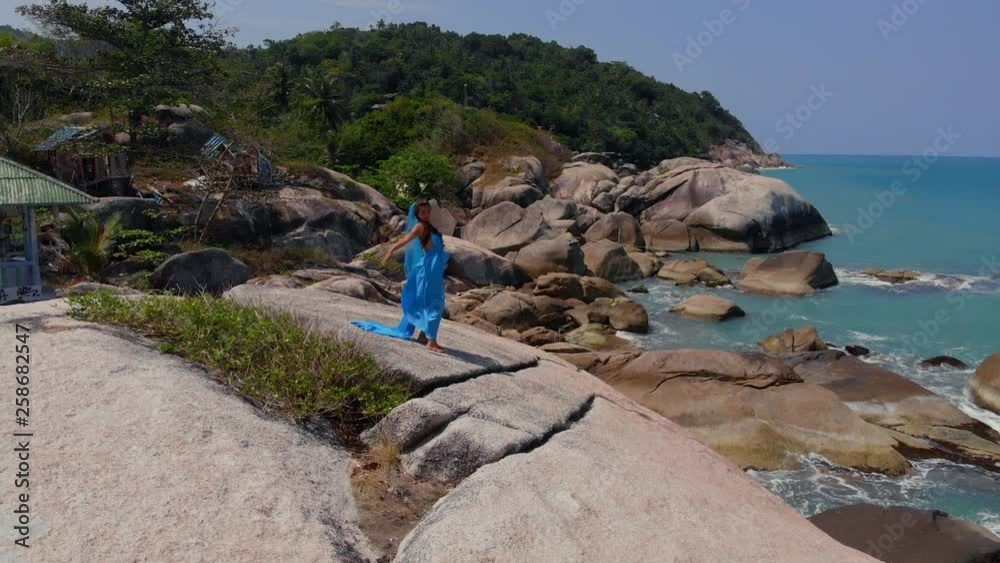 Aerial drone view of beautiful brunette girl in blue long dress dancing ...