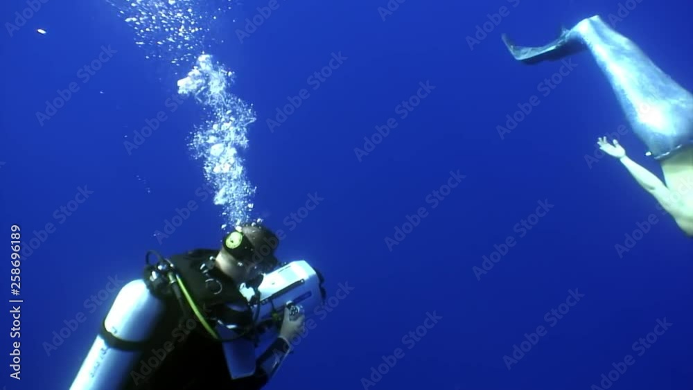 Cameraman shoots mermaid underwater on clean blue background in sea ...
