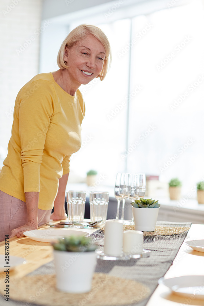 Happy beautiful mature woman with blond hair leaning on table and ...