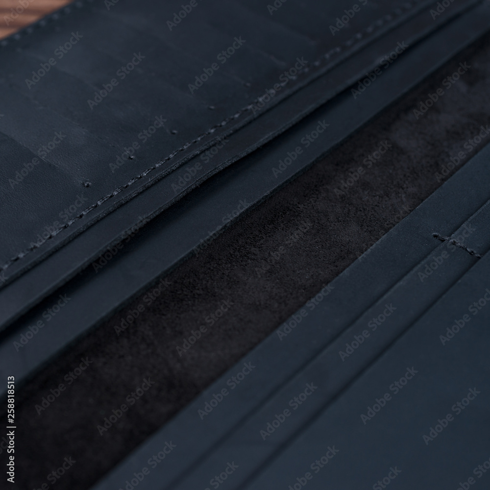Part of handmade black travel wallet lies on textured wooden backgroud ...