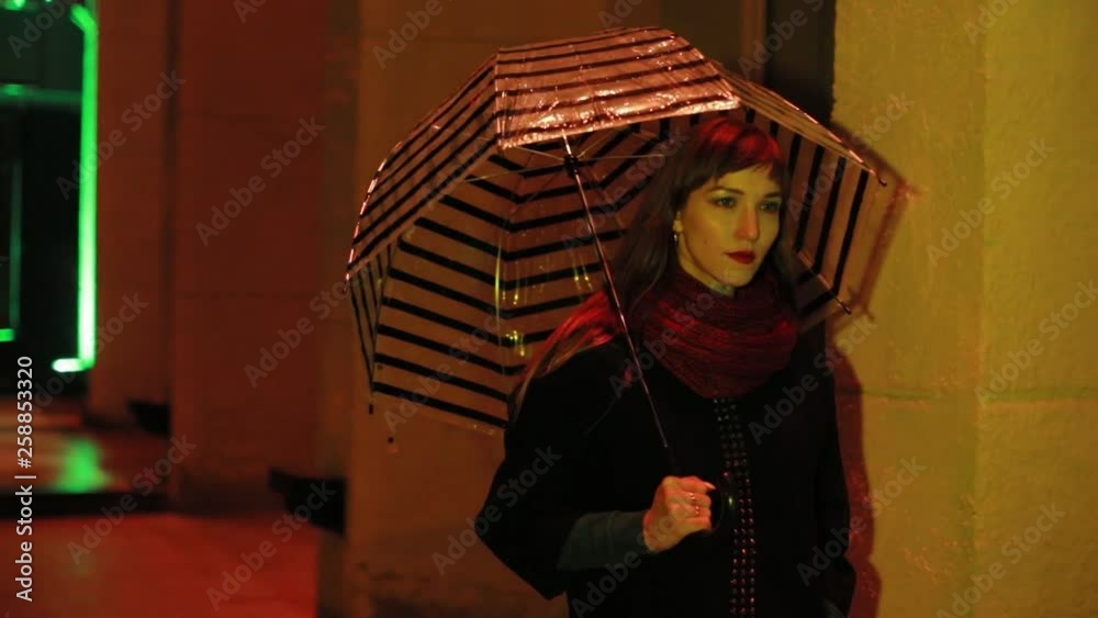 A young beautiful girl is lit by the glowing neon lights of the night ...