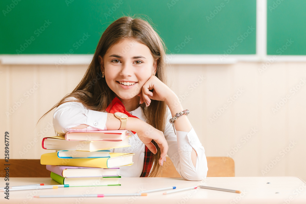 girl in school uniform sitting at her desk in the classroom with books ...