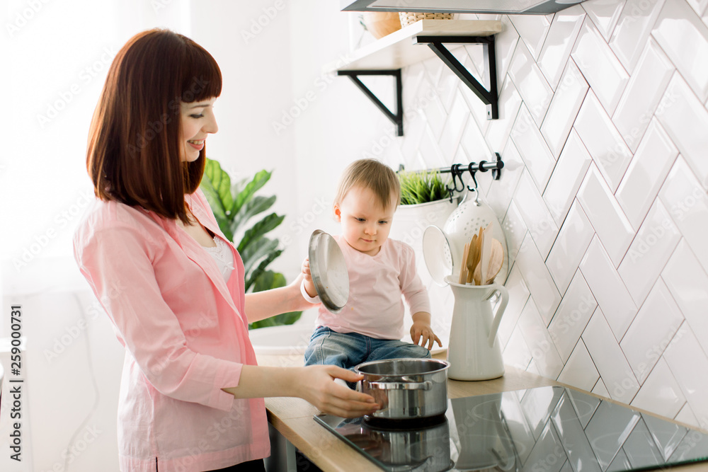 Mother with her little baby daughter in the kitchen cooking together ...
