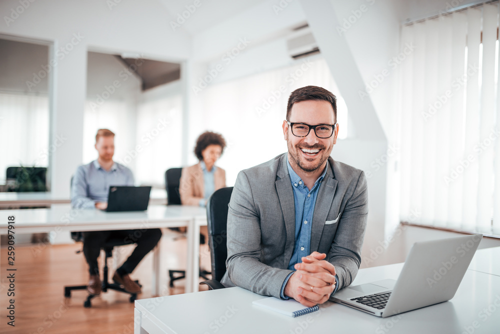Cheerful young man sitting in office with laptop. Stock Photo | Adobe Stock