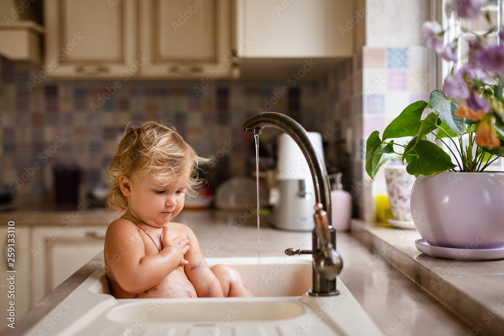 baby-taking-bath-in-kitchen-sink-child-playing-with-water-and-soap
