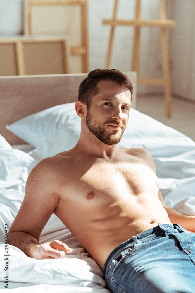 Handsome And Shirtless Man Lying On Bed And Looking At Camera In