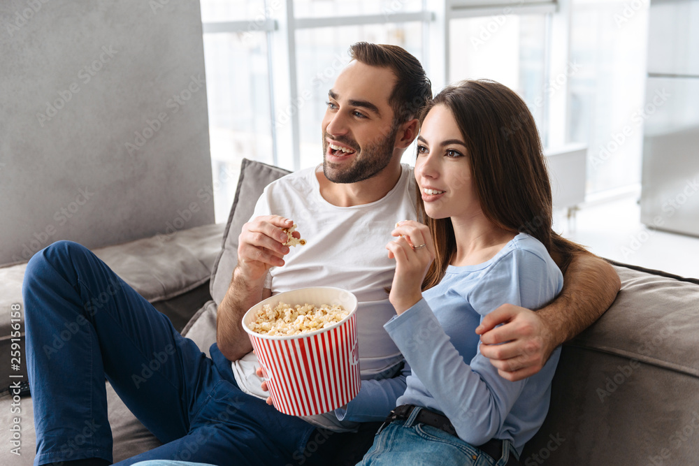 Image of adorable couple eating popcorn from bucket while sitting on ...