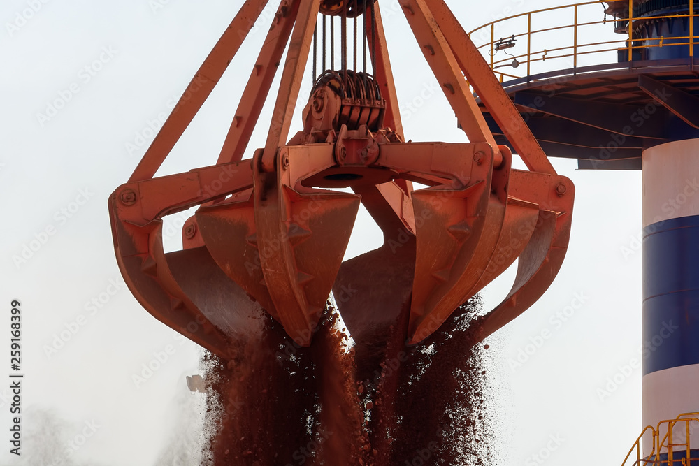 Low angle view of crane grabber with bauxite ore against bleached sky ...