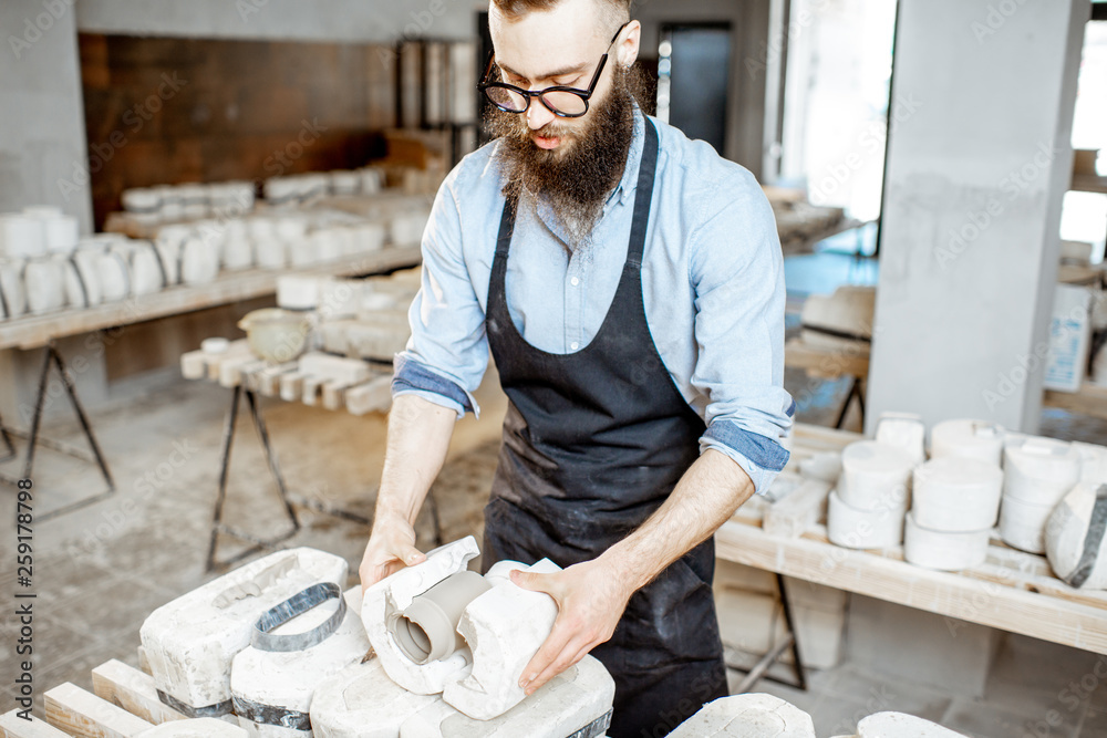 Handsome worker in apron getting clay products from the gypsum forms at ...