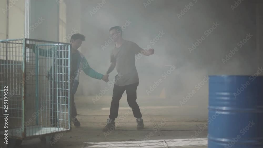 Two young men dancing in the dark and dusty room of abandoned building ...