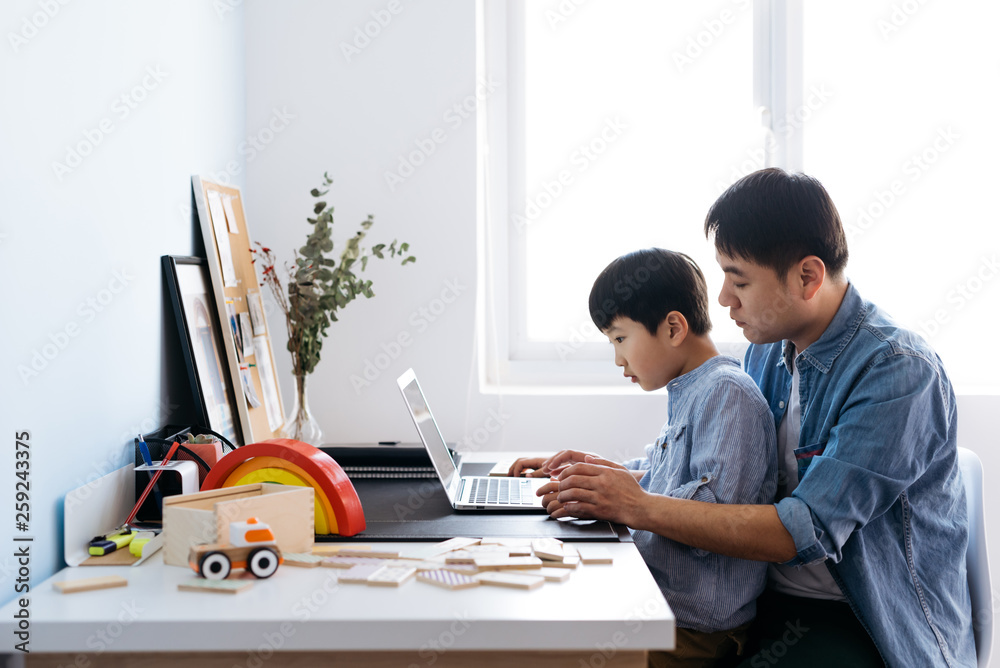 Boy sitting on father's lap behind desk in home office Stock Photo ...