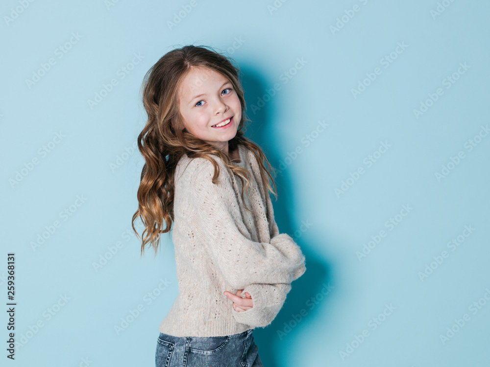 pretty and cool 9 year old girl with brown wool sweater posing in front of blue background Stock ...