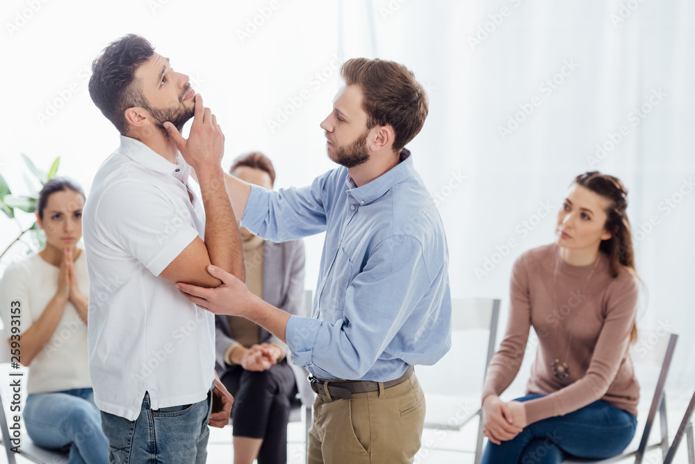 man consoling another man while people sitting on chairs during group ...