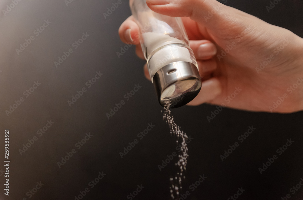 Sprinkle salt from a jar on a black background. Hand with a can of salt ...