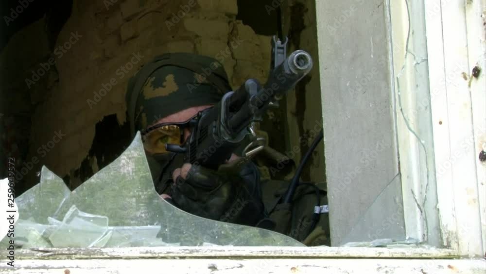 Soldier in military uniform with guns is firing from window of ruined ...
