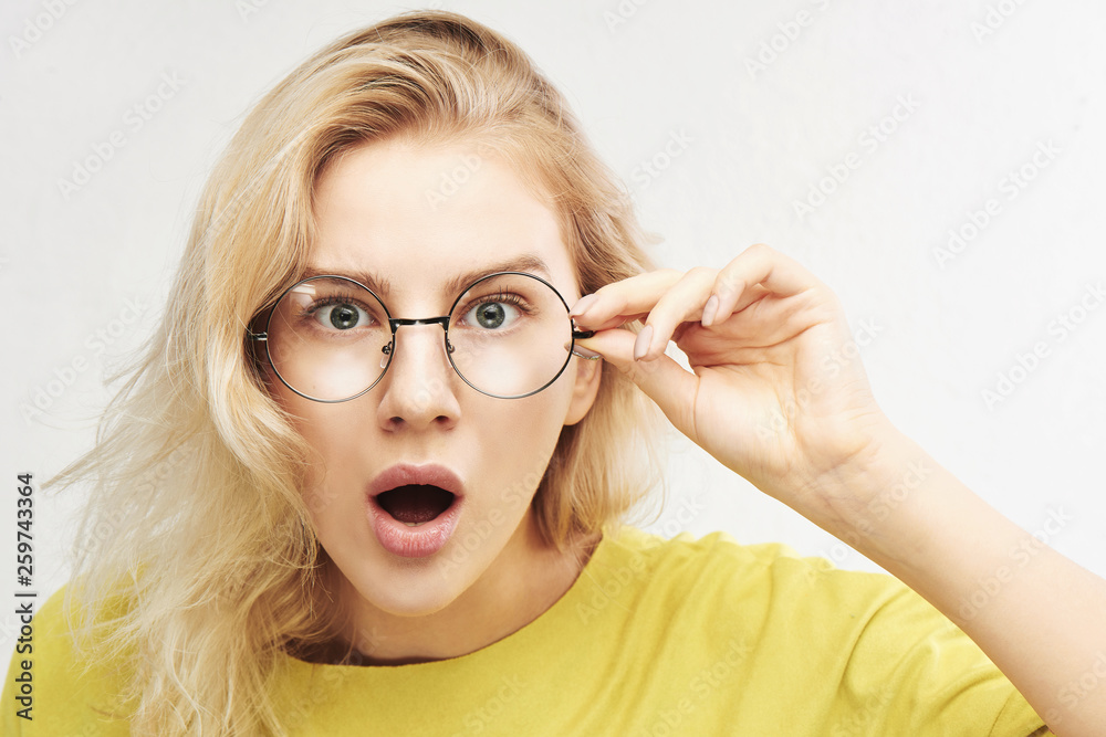 Surprised woman in round glasses with open mouth and bulging eyes looks ...