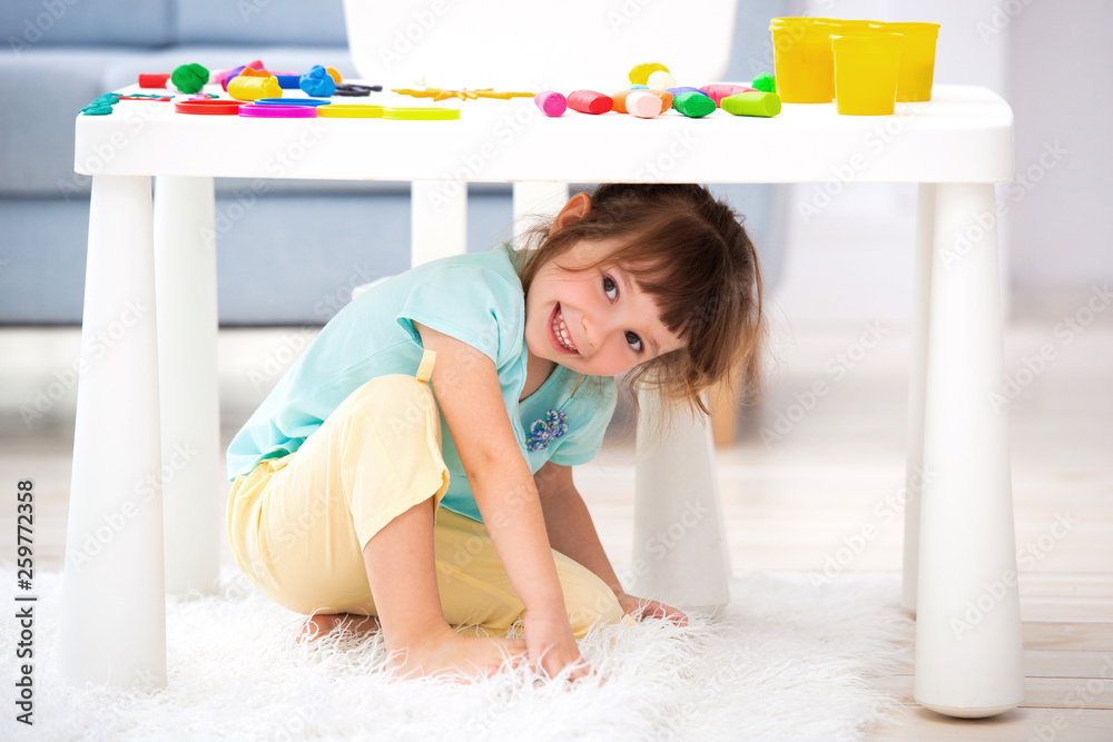 Little cute girl crawled under the table. The kid smiles, plays hide ...