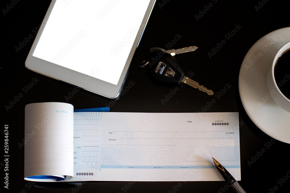 Mockup image of checkbook,pen, digital tablet with blank white screen and car key on dark table ...