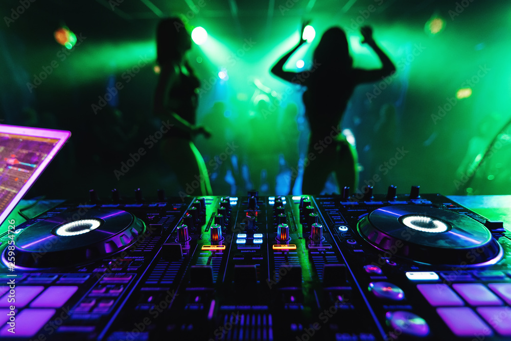 DJ mixer in a nightclub with dancing on the background of go-go dance ...