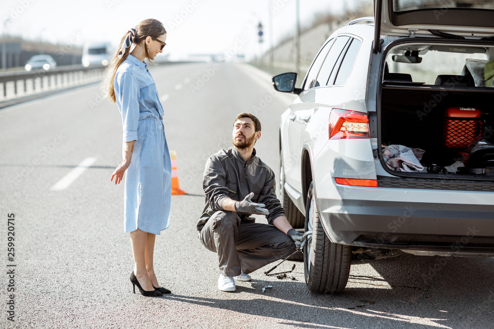 Road assistance worker helping young woman to change a car wheel on the ...