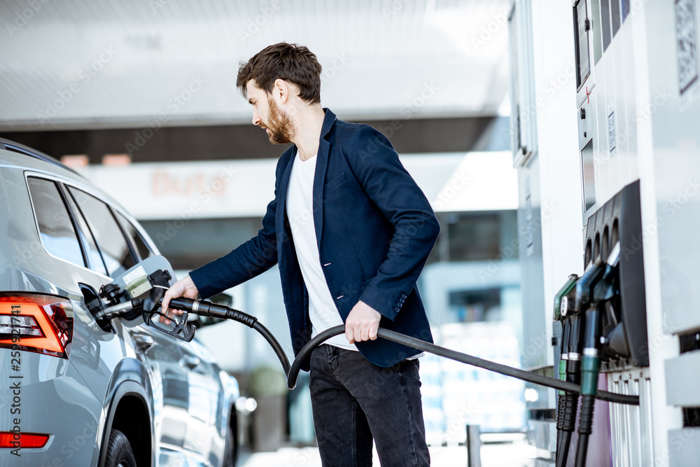 Foto de Businessman refueling his luxury car holding filling gun at the ...