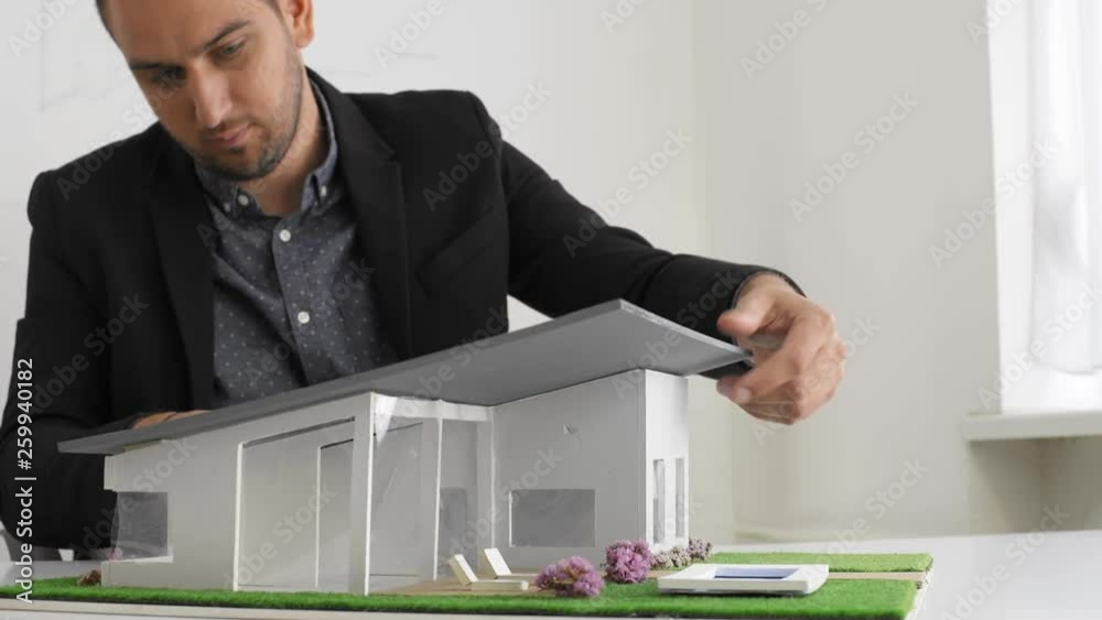 Businessman fixes the architecture of a house model with swimming pool ...