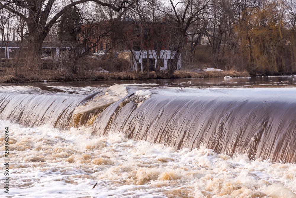 Fast moving river water flowing over concrete dam. Ice floes and chunks ...