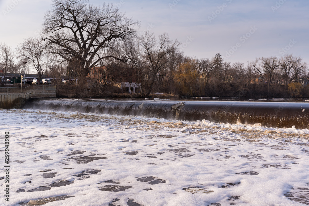 Fast moving river water flowing over concrete dam. Ice floes and chunks ...