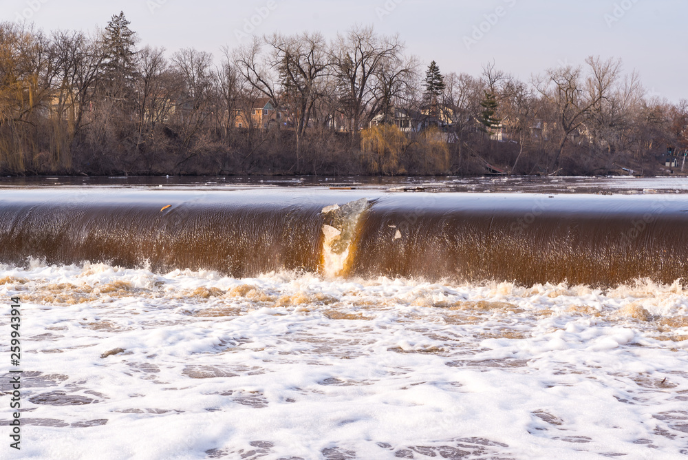 Fast moving river water flowing over concrete dam. Ice floes and chunks ...
