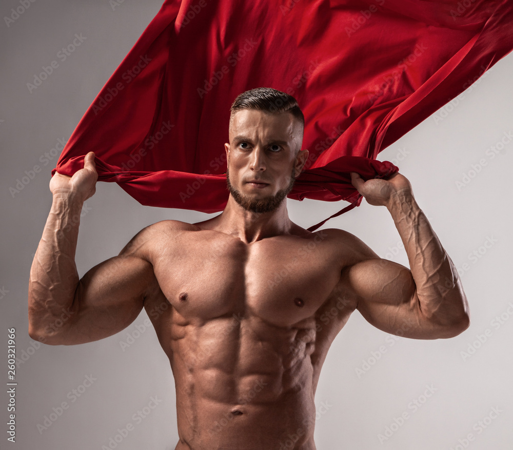 Male bodybuilder puts on his shoulders a red cloak with a serious face ...