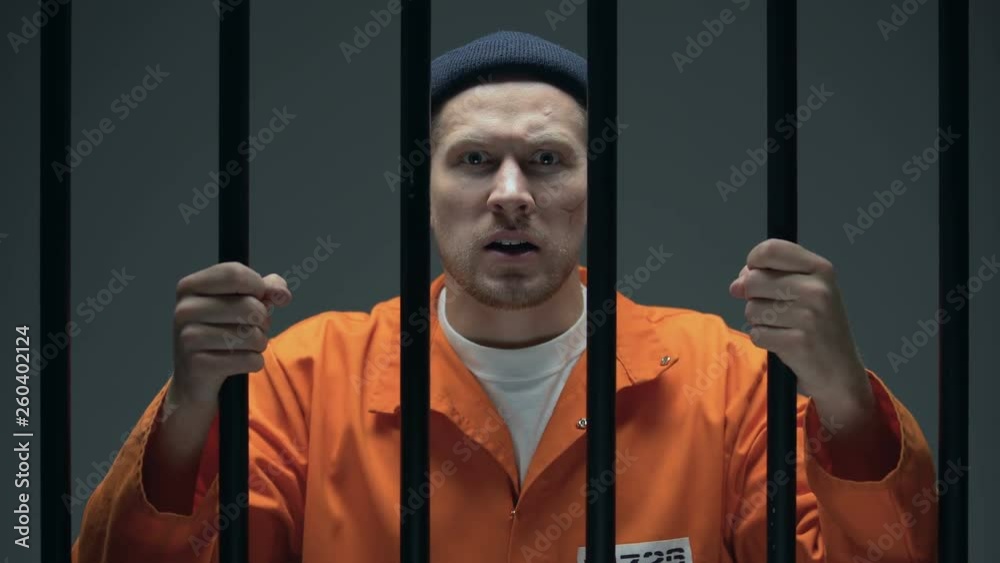 Aggressive dangerous male prisoner with scar on face holding bars and ...