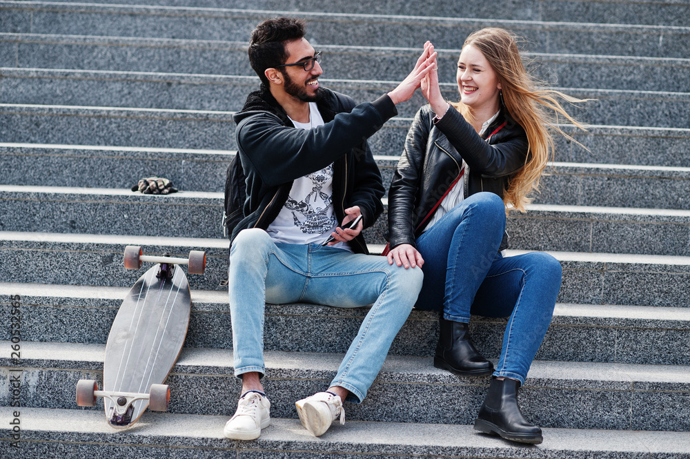 Cool multiracial couple sitting on stairs with longboard and give high ...