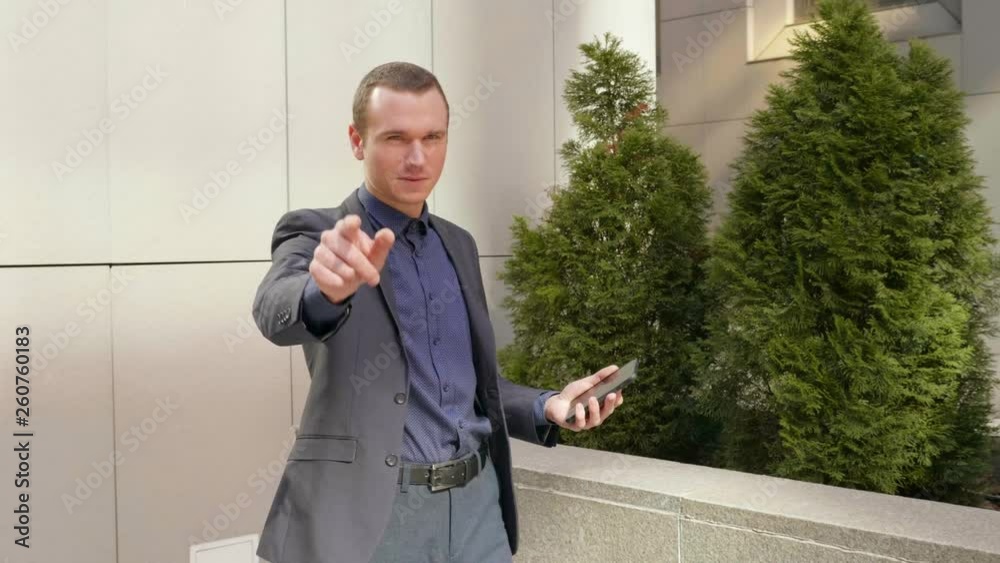 A young businessman is standing on the street pointing his finger at ...