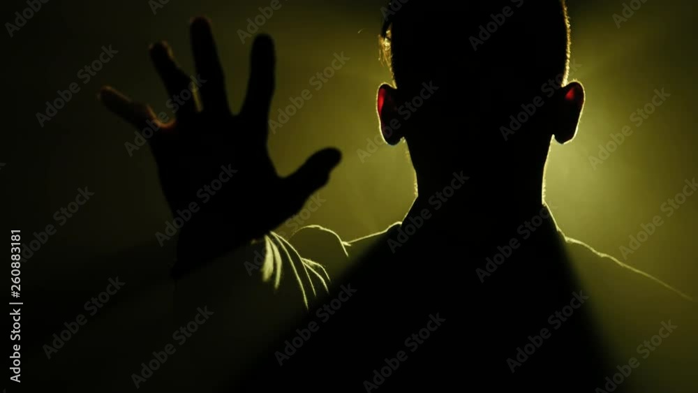 Slihouette of young man in the dark smoky room. He slowly rising his ...