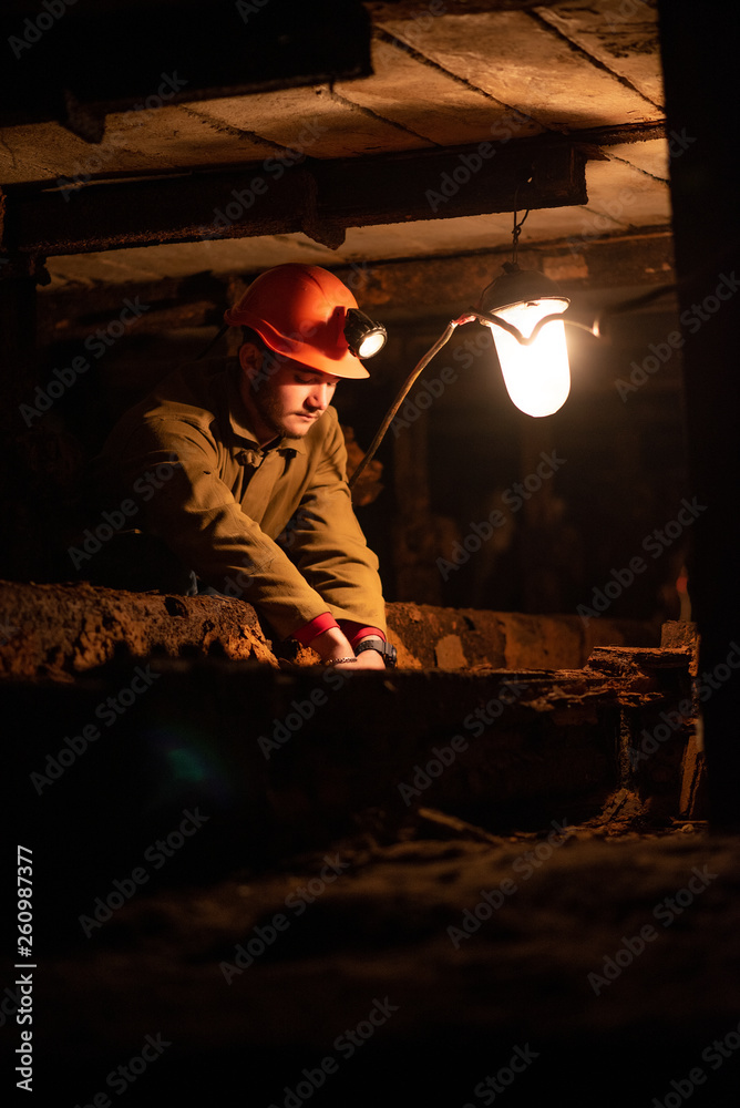 young guy in a working uniform and protective helmets, sitting in a low ...
