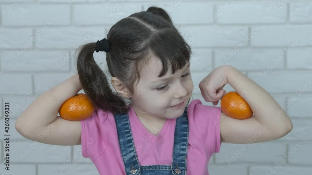 Kid shows biceps. Cute little girl with tangerines shows biceps. Strong ...