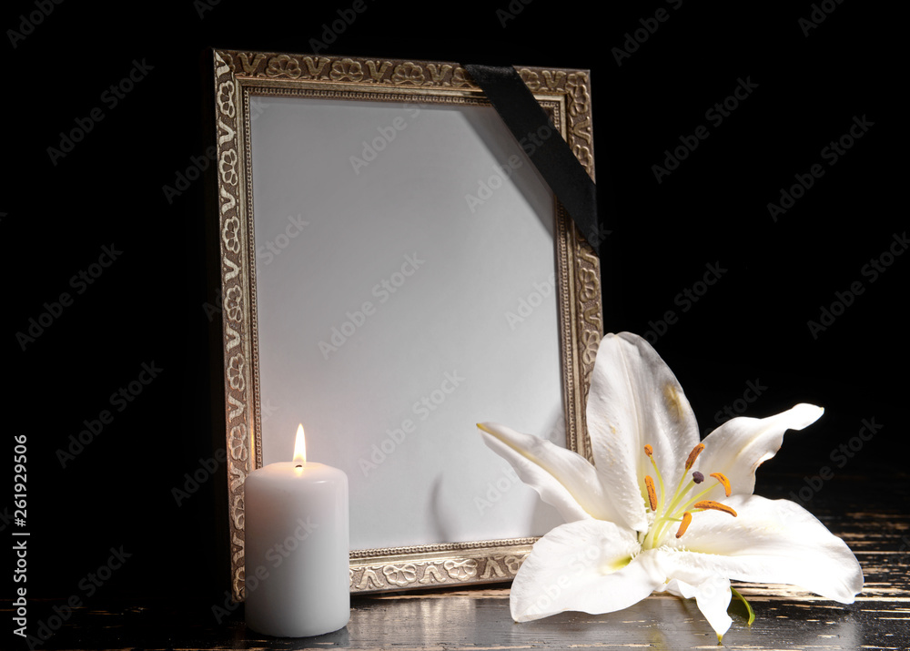 Blank funeral frame, burning candle and flower on table against dark ...