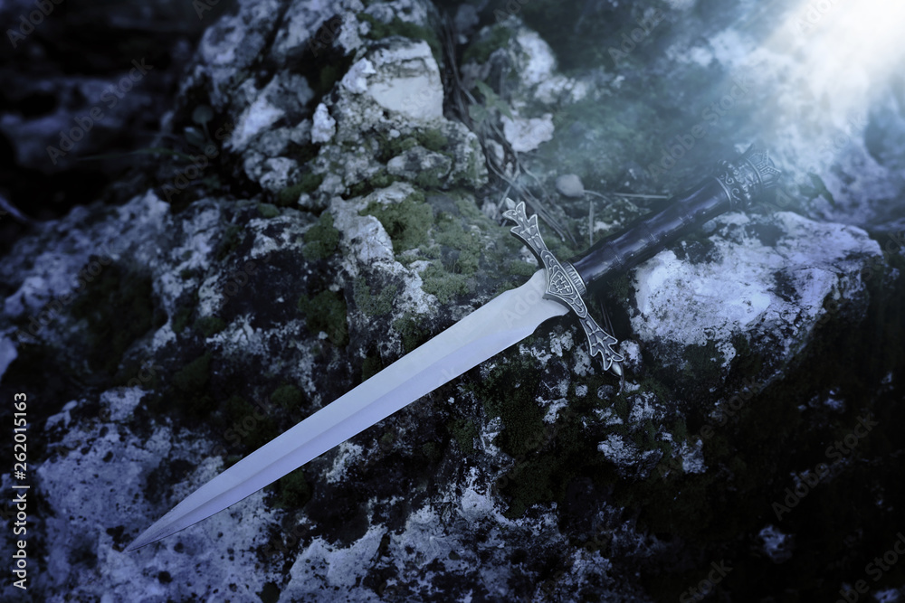 mysterious and magical photo of silver sword over the stone covered ...