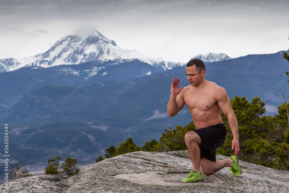 Fit and Muscular Young Man is doing exercises on top of the Mountain ...