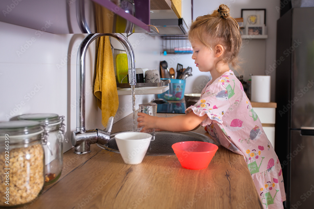 The cute and adorable girl fills a glass with water from a water tap in ...