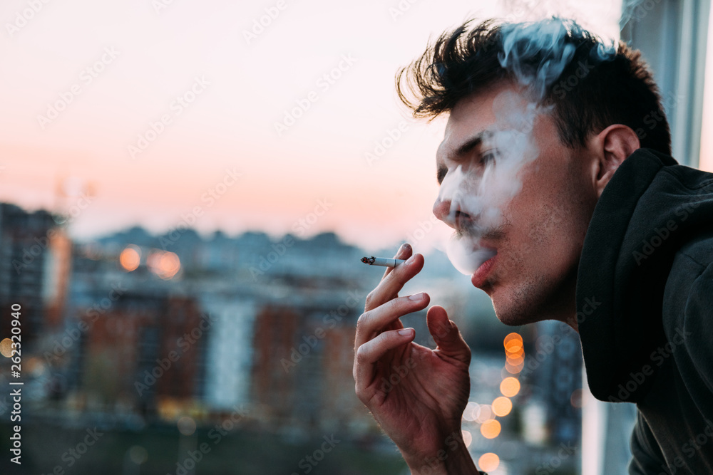 Young man smoking a cigarette on the balcony in sunset Stock Photo ...