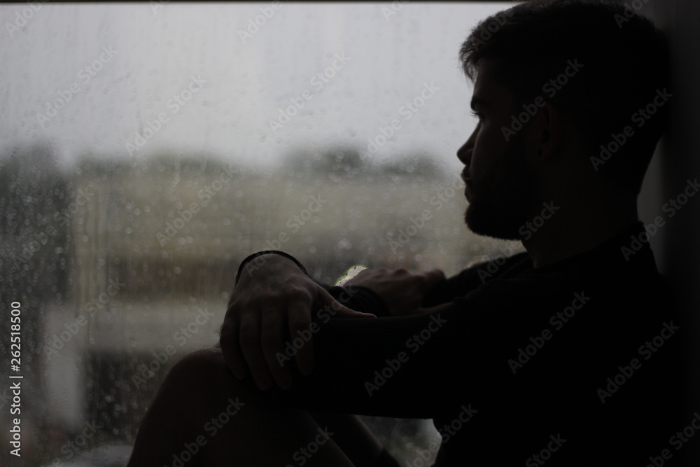 silhouette of a man sitting in the window with rain in mood of sadness ...