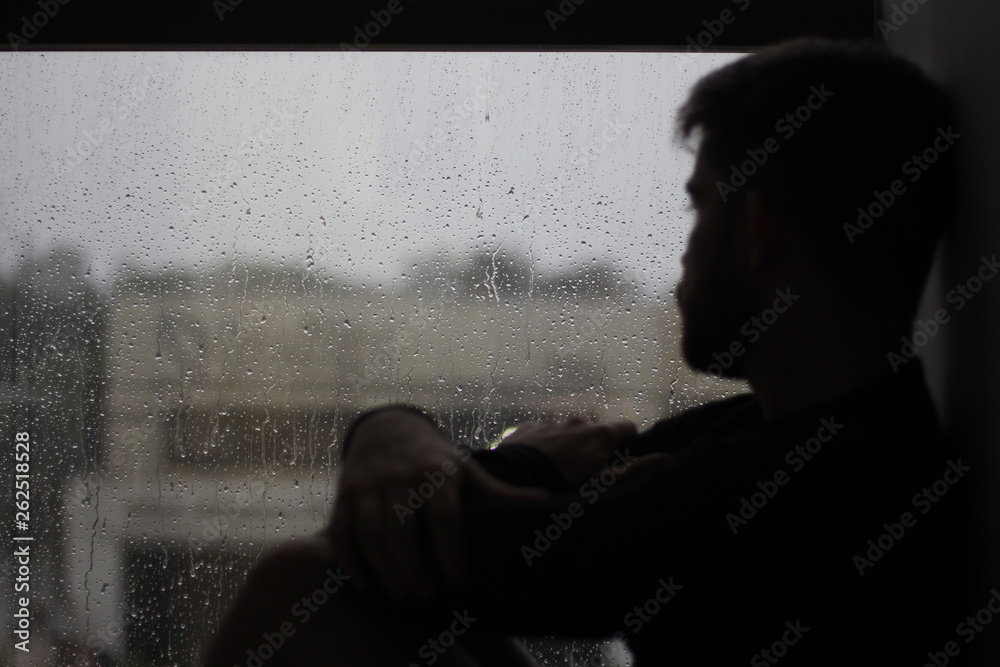 silhouette of a man sitting in the window with rain in mood of sadness ...