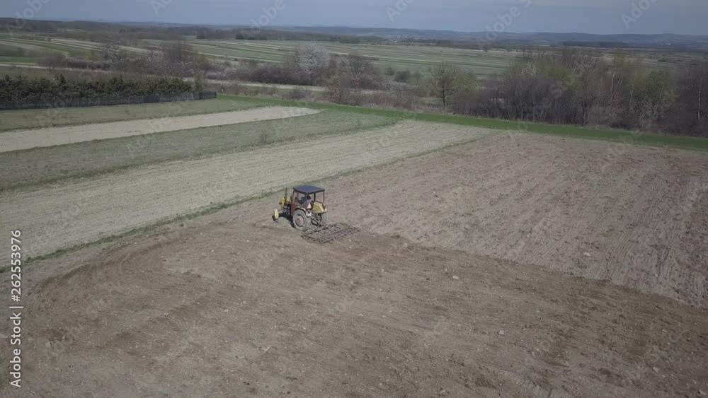 A farmer on a tractor with a seeder sows grain in plowed land in a ...
