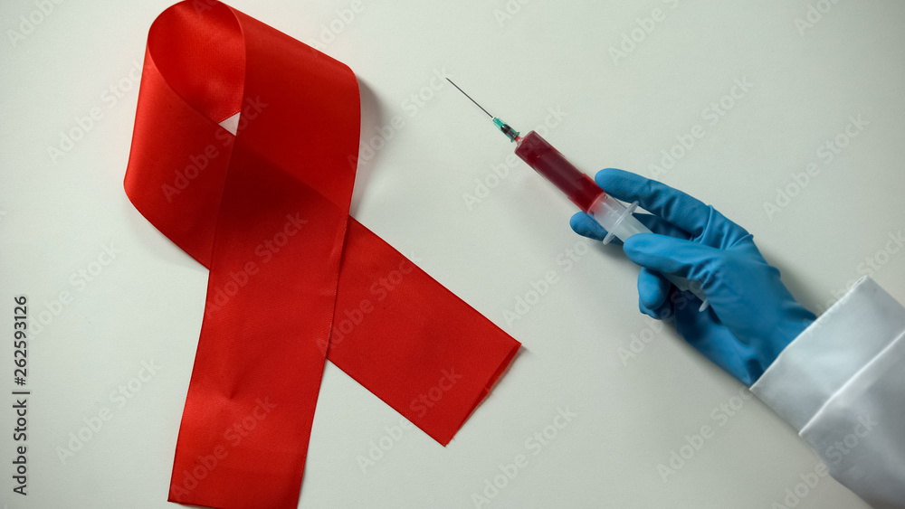 Red ribbon and syringe with blood sample on table, AIDS diagnostics ...