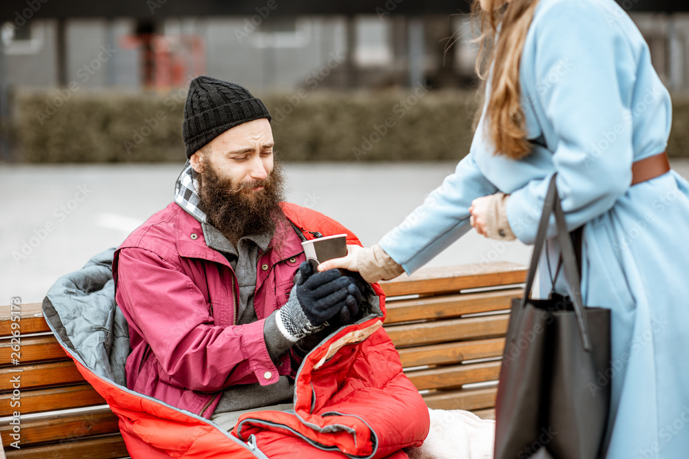 Woman helping homeless beggar giving some hot drink outdoors. Concept ...
